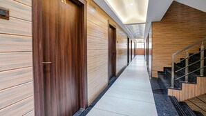 Corredor moderno de hotel com painéis de madeira, portas numeradas e escada com corrimãos de metal.