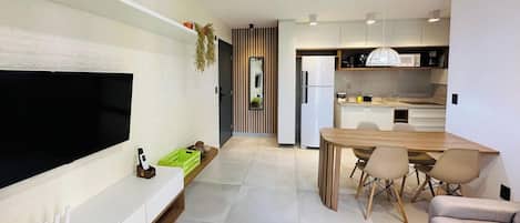 Cozinha moderna com área de refeições, televisão de tela plana na parede e mesa de madeira com cadeiras.