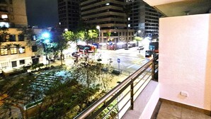 Vista noturna de uma varanda com vista para uma rua movimentada, com edifícios e árvores.