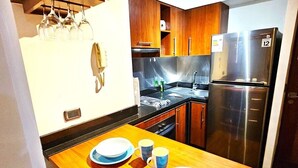 Uma cozinha compacta com armários de madeira, uma geladeira de aço inoxidável e uma mesa de jantar de madeira posta com pratos e xícaras.