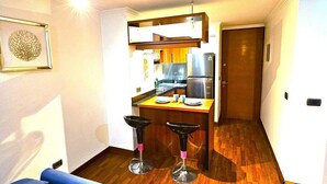 Um espaço compacto para viver com cozinha compacta, um sofá azul e dois banquetes pretos.