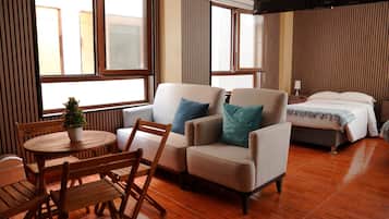 Quarto de hotel com uma cama, duas poltronas, uma mesa de madeira e um vaso de planta.