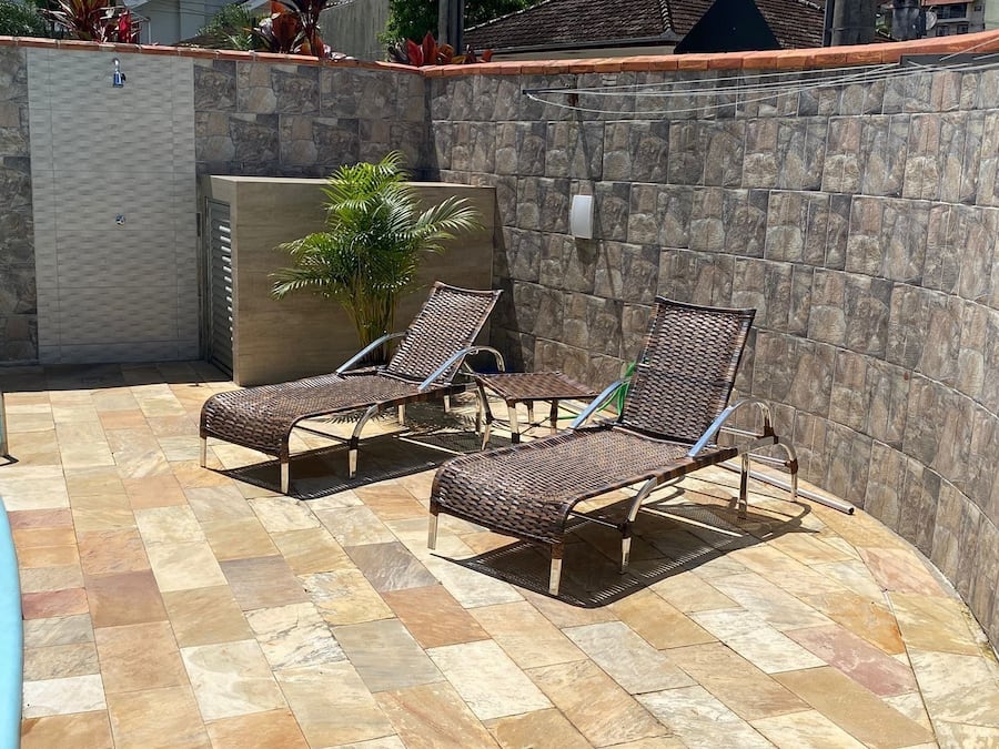 Área da piscina com duas espreguiçadeiras de vime e um muro de pedra.