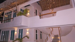 Um edifício com vários andares, paredes brancas, varandas de madeira e luzes de corda.
