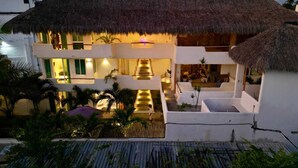 Uma casa moderna com telhado de palha, uma escadaria central e área de piscina.
