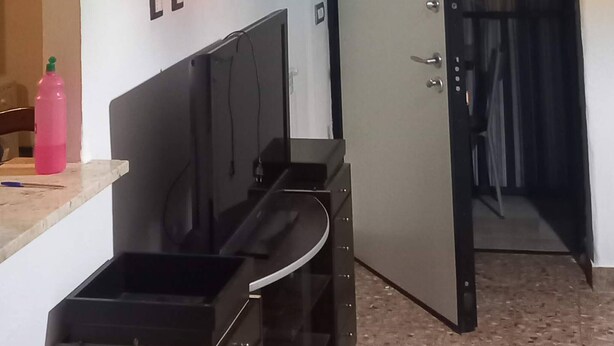 Quarto de hotel com televisão, guarda-roupa, porta e luminária na parede.