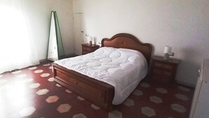 Quarto com cama de madeira, duas mesas de cabeceira, um criado-mudo e um espelho.