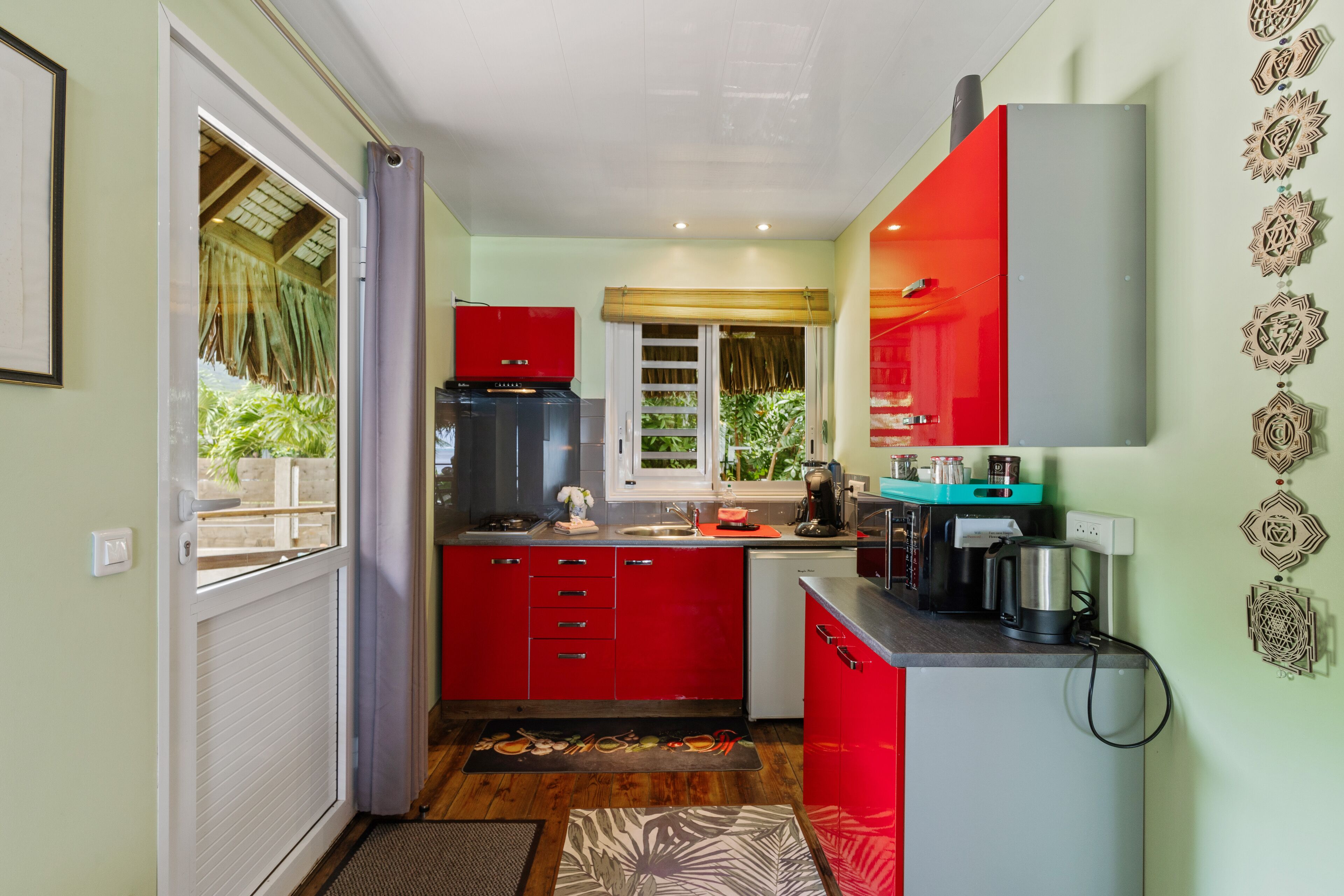 Cozinha compacta com armários vermelhos, cafeteira e janela com vista para o verde.
