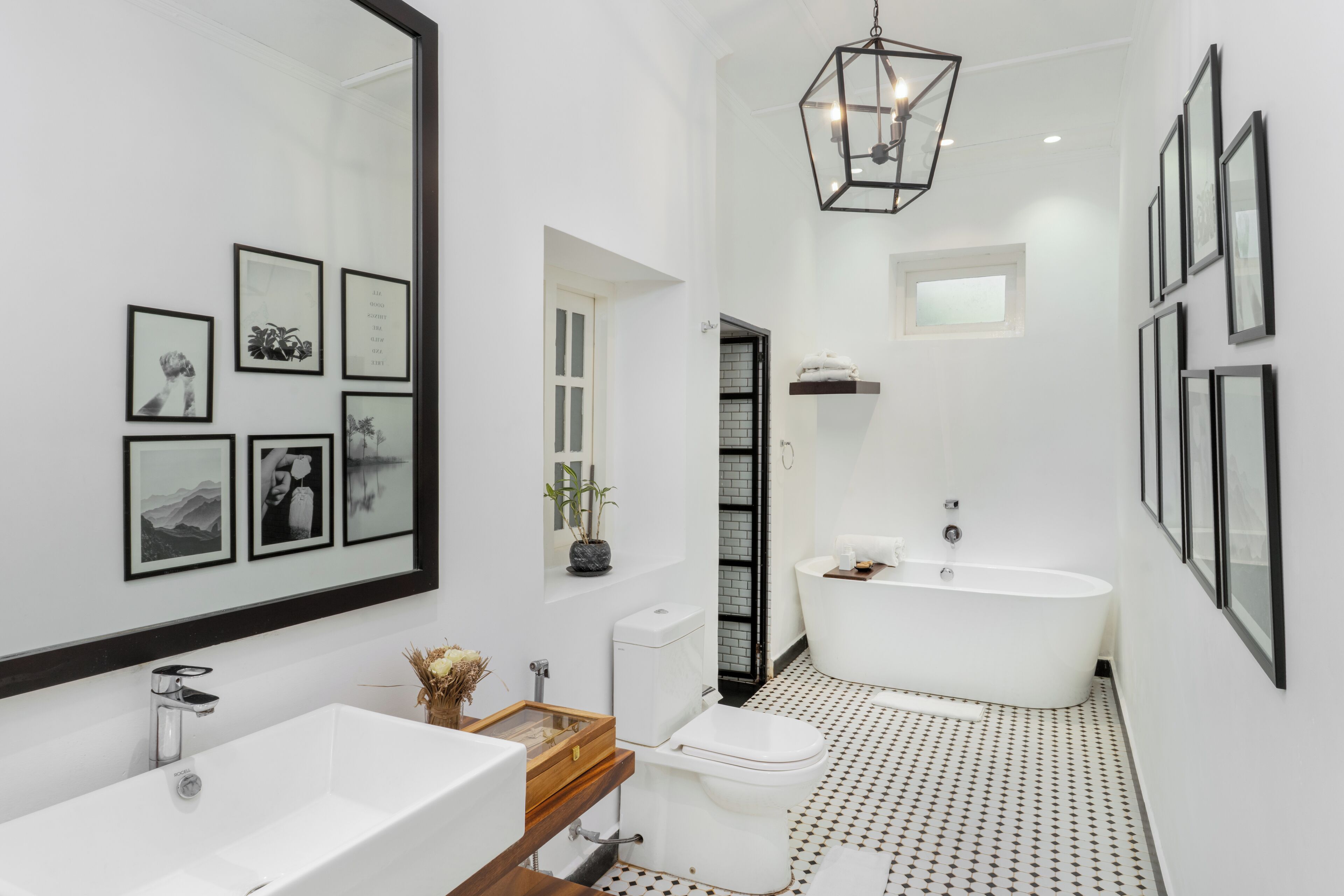 Um banheiro moderno com um espelho grande, quadros emoldurados, uma banheira separada e um vaso sanitário.