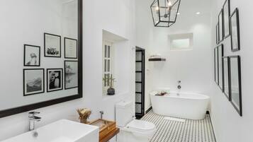 Um banheiro moderno com um espelho grande, quadros emoldurados, uma banheira separada e um vaso sanitário.