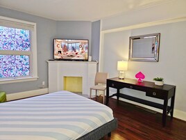 Quarto com cama, lareira, televisão, escrivaninha e espelho.