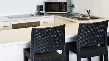 Uma cozinha com micro-ondas, cafeteira e pia. Há duas cadeiras de vime no balcão.