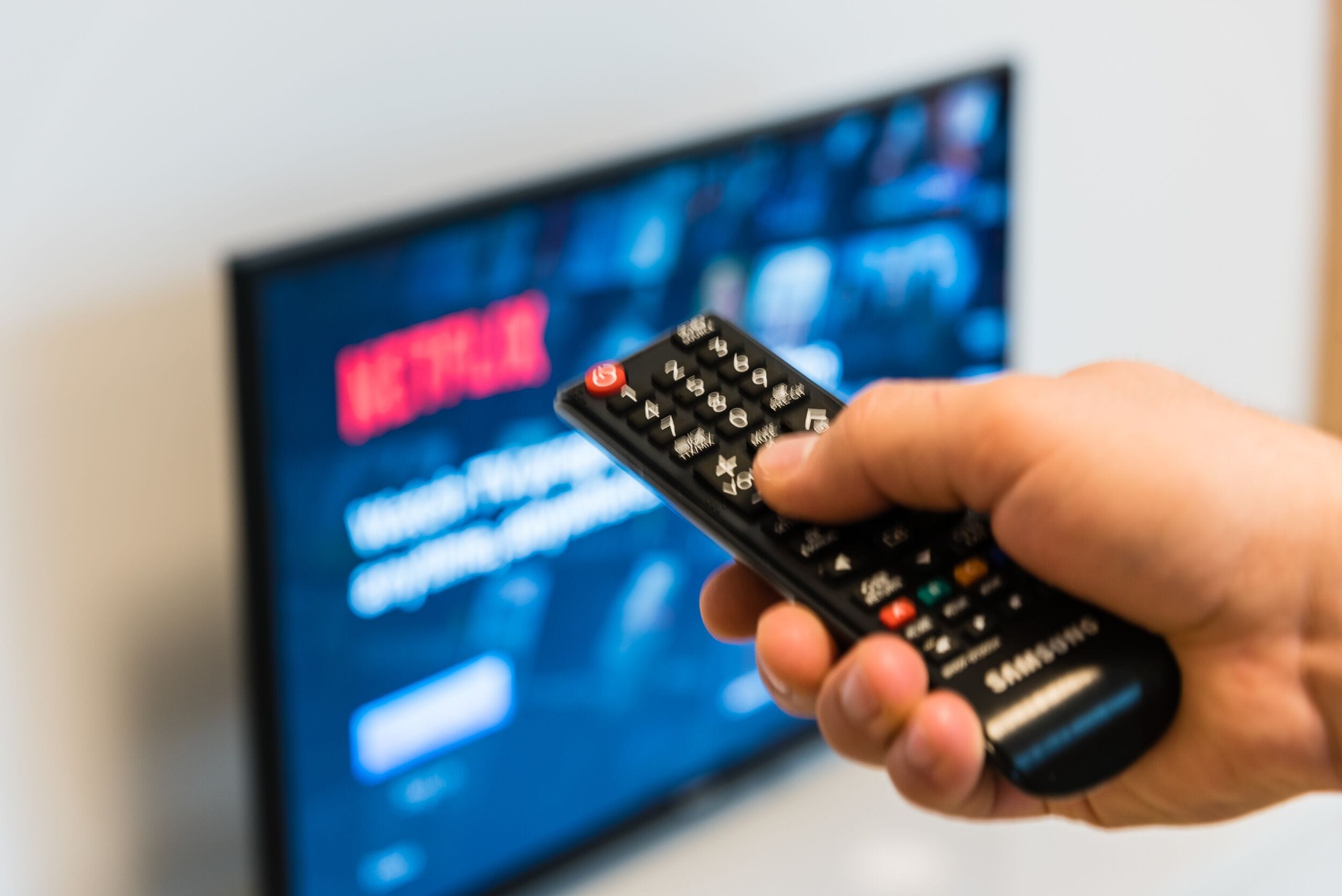 Mão segurando um controle remoto em frente a uma televisão exibindo um menu.