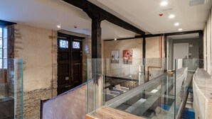Um interior moderno com paredes de pedra aparente, guarda-corpo de vidro e uma escadaria que desce para um nível inferior.