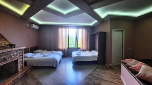 Quarto de hotel com duas camas, um banco de madeira, uma mesa pequena e vista para o verde lá fora.