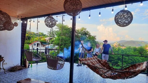Um terraço amplo com cadeiras de vime suspensas, um banco de madeira e vista para uma paisagem exuberante.