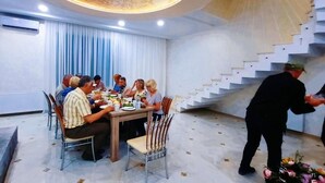 Uma área de refeições com uma mesa redonda, cadeiras e uma pessoa servindo comida.