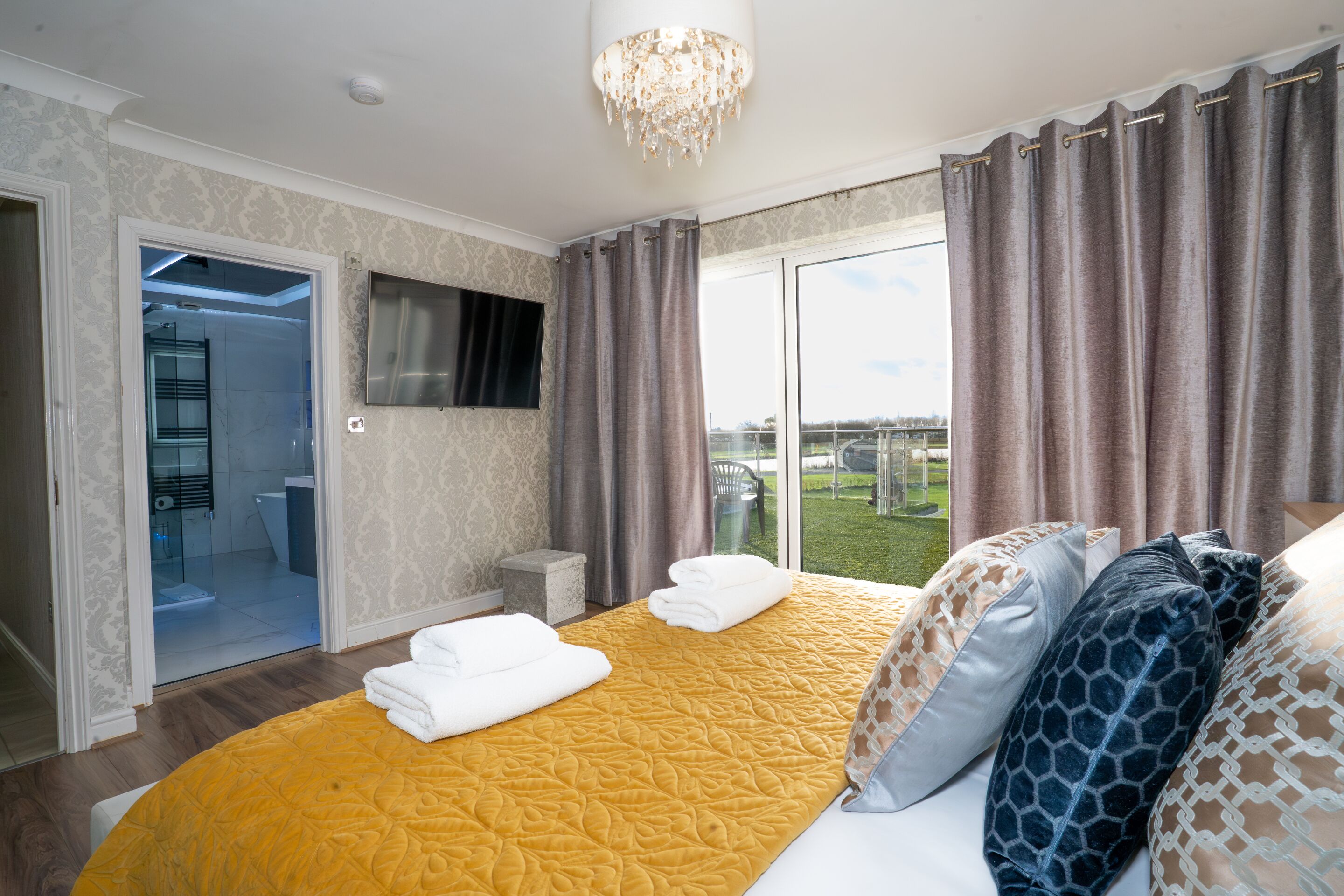 Quarto de hotel com uma cama grande, televisão de tela plana, banheiro com porta de vidro e vista para o exterior.