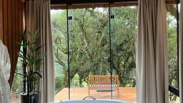 Casa de banho moderna com uma banheira grande, teto de madeira e vista para um deck de madeira e vegetação lá fora.
