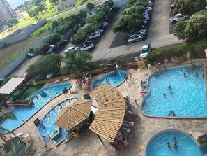 Área de piscina no terraço com várias piscinas, guarda-sóis e um estacionamento.