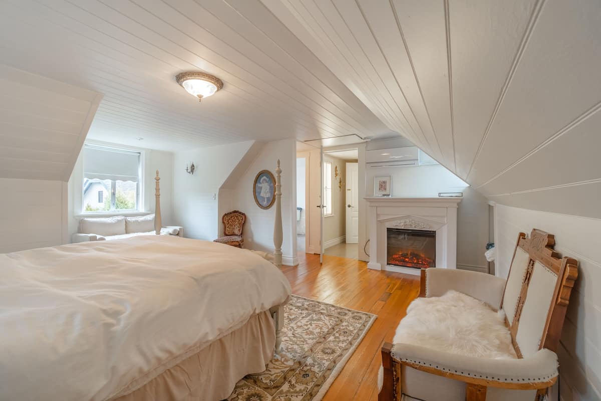Quarto com cama grande, uma cadeira, lareira e vista para o exterior.