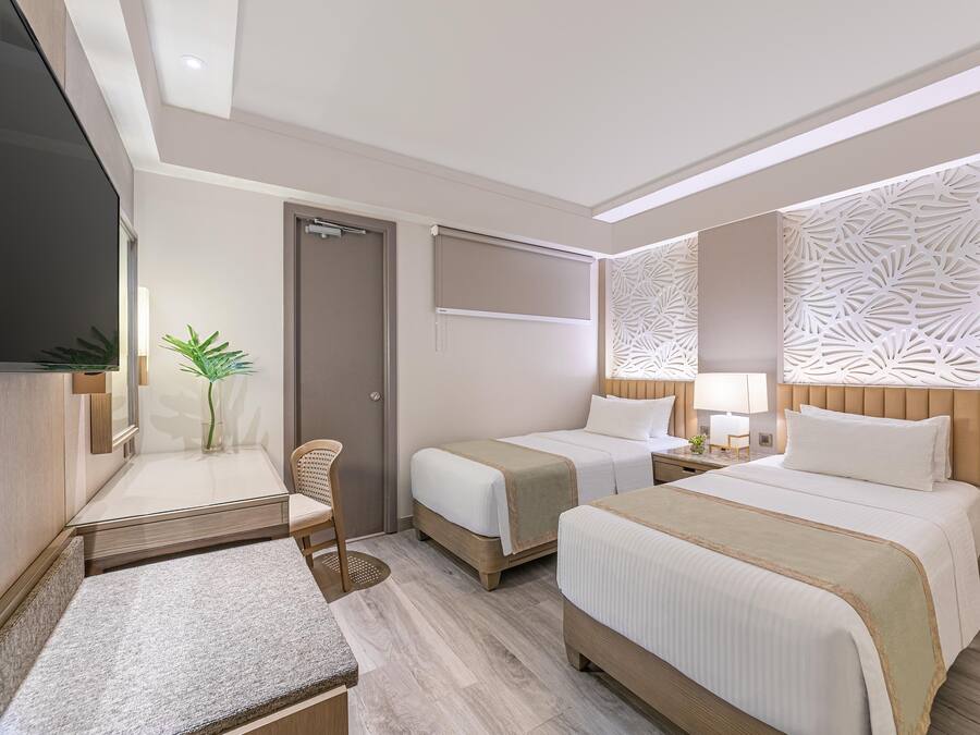 Quarto de hotel com duas camas, televisão, escrivaninha e uma cadeira.