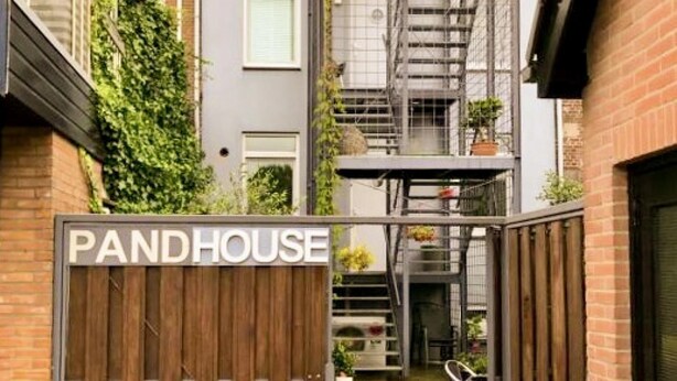 Uma casa moderna com portão de madeira com a placa 'PANDHOUSE', escadas e uma pequena área de jardim.