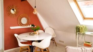 Uma sala de jantar com uma mesa redonda, cadeiras brancas e uma parede com detalhes vermelhos.