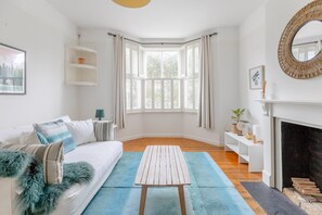 Uma sala de estar moderna com um sofá branco, um tapete azul, uma mesa de centro de madeira, uma lareira e uma janela saliente com cortinas.