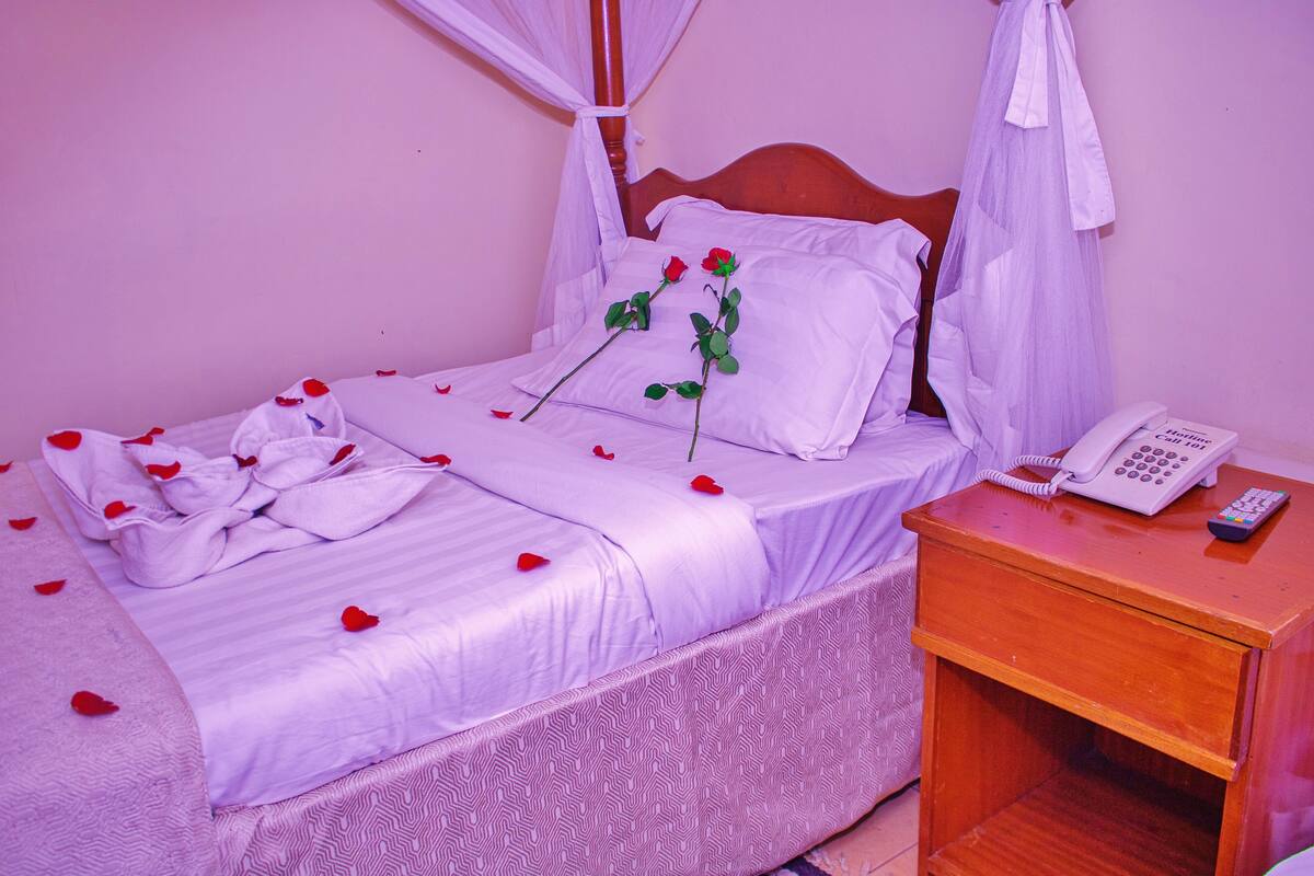 Uma cama com edredão branco, cabeceira de madeira e mesa de cabeceira com telefone e controle remoto.