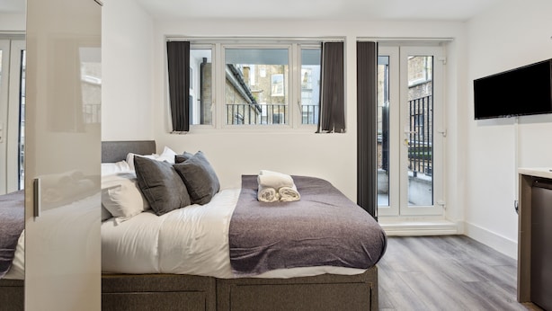 Quarto moderno com uma cama grande, televisão e varanda com vista para a cidade.