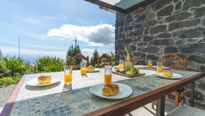 Mesa posta com croissants, suco e frutas, com vista panorâmica.