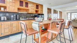 Cozinha moderna com armários de madeira, uma ilha central com banquetas e uma janela grande que traz luz natural.