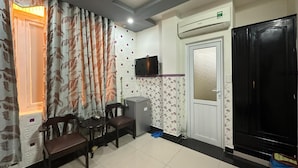 Quarto com área de refeições, televisão fixada na parede, porta com painel de vidro jateado e aparelho de ar condicionado.