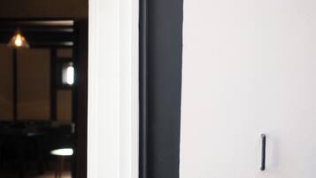Uma porta dá acesso a um ambiente com pouca luz, onde se veem uma mesa e cadeiras.