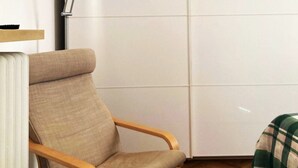 Um quarto com uma cadeira de madeira, um abajur e um guarda-roupa branco.