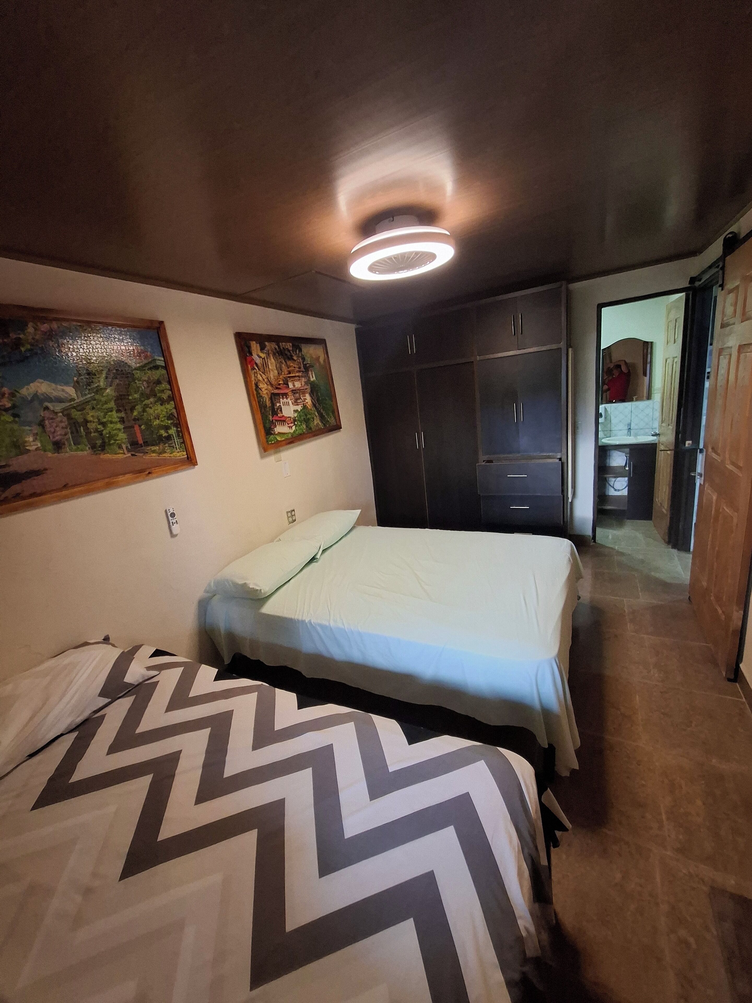 Quarto com cama, guarda-roupa, um quadro e banheiro visível por uma porta aberta.
