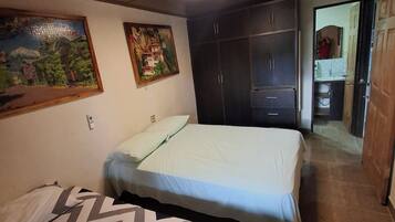 Quarto com cama, guarda-roupa, um quadro e banheiro visível por uma porta aberta.