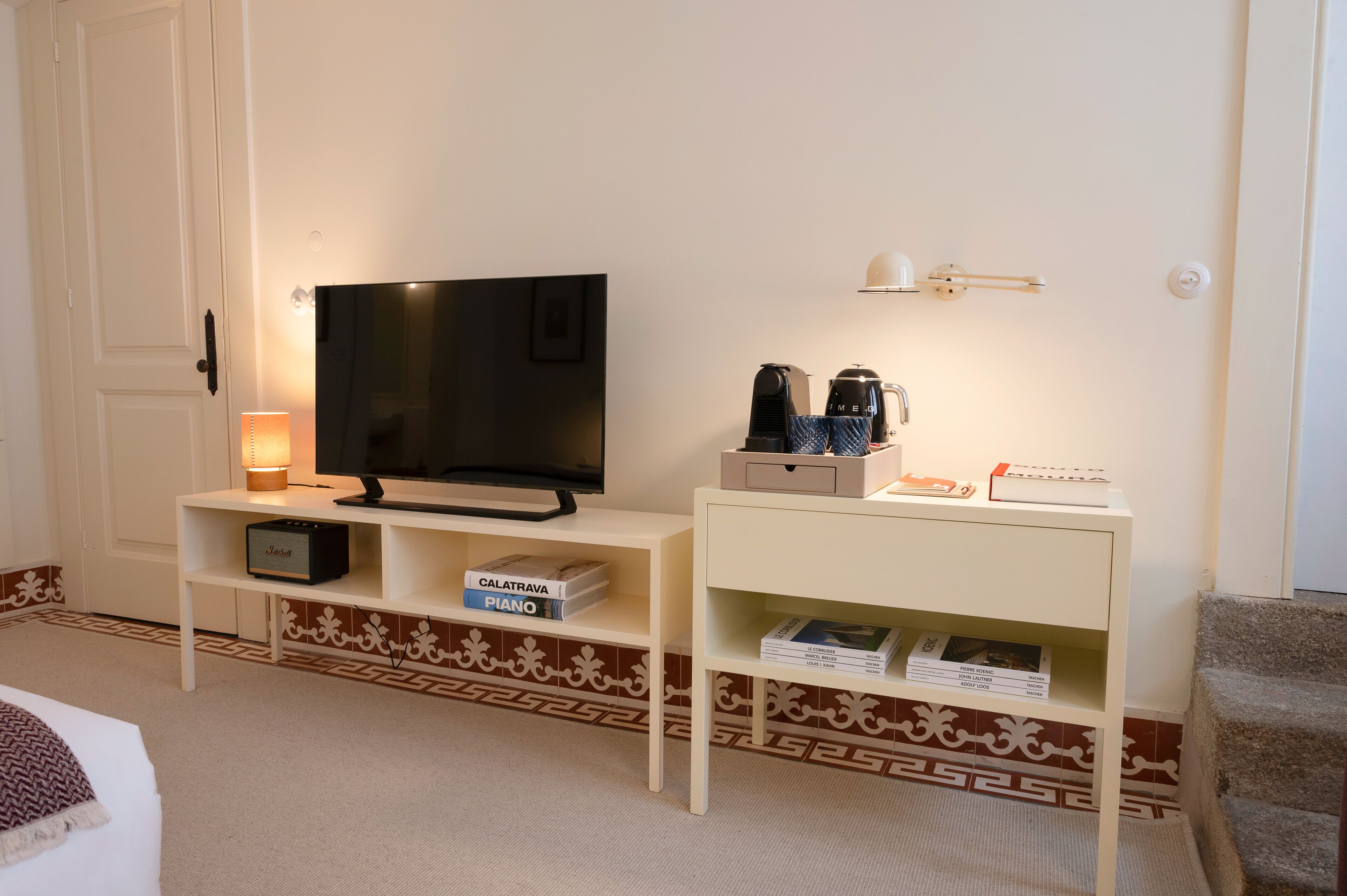Sala de estar com televisão, cafeteira e livros sobre uma mesa consola branca.