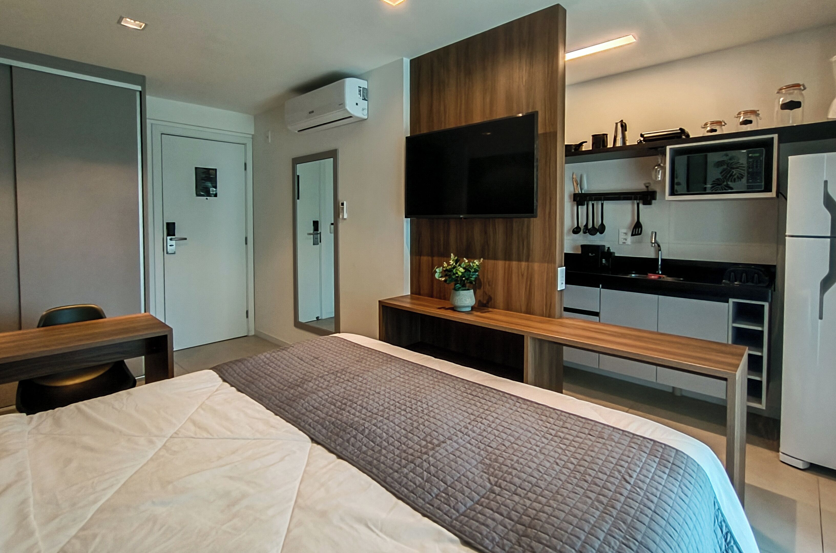 Quarto de hotel com cama, escrivaninha, cozinha compacta e televisão.
