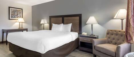 Quarto de hotel com uma cama grande, duas mesas de cabeceira com luminárias, uma poltrona e um telefone fixado na parede.