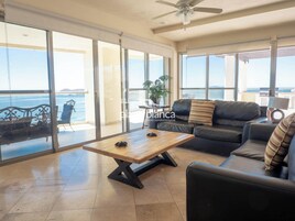 Uma sala de estar espaçosa com uma grande porta de vidro deslizante que dá para uma varanda com vista para o mar.