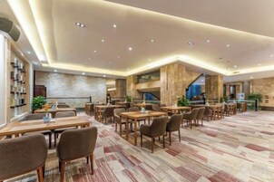 Ampla sala de jantar de hotel com várias mesas e cadeiras, carpete estampado e design de teto moderno.