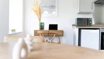Uma cozinha com micro-ondas, mini geladeira, escrivaninha de madeira com laptop e um vaso com plantas secas.