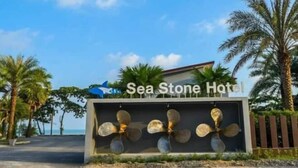 Placa do Hotel Sea Stone, com um painel decorativo de leques e palmeiras ao fundo.