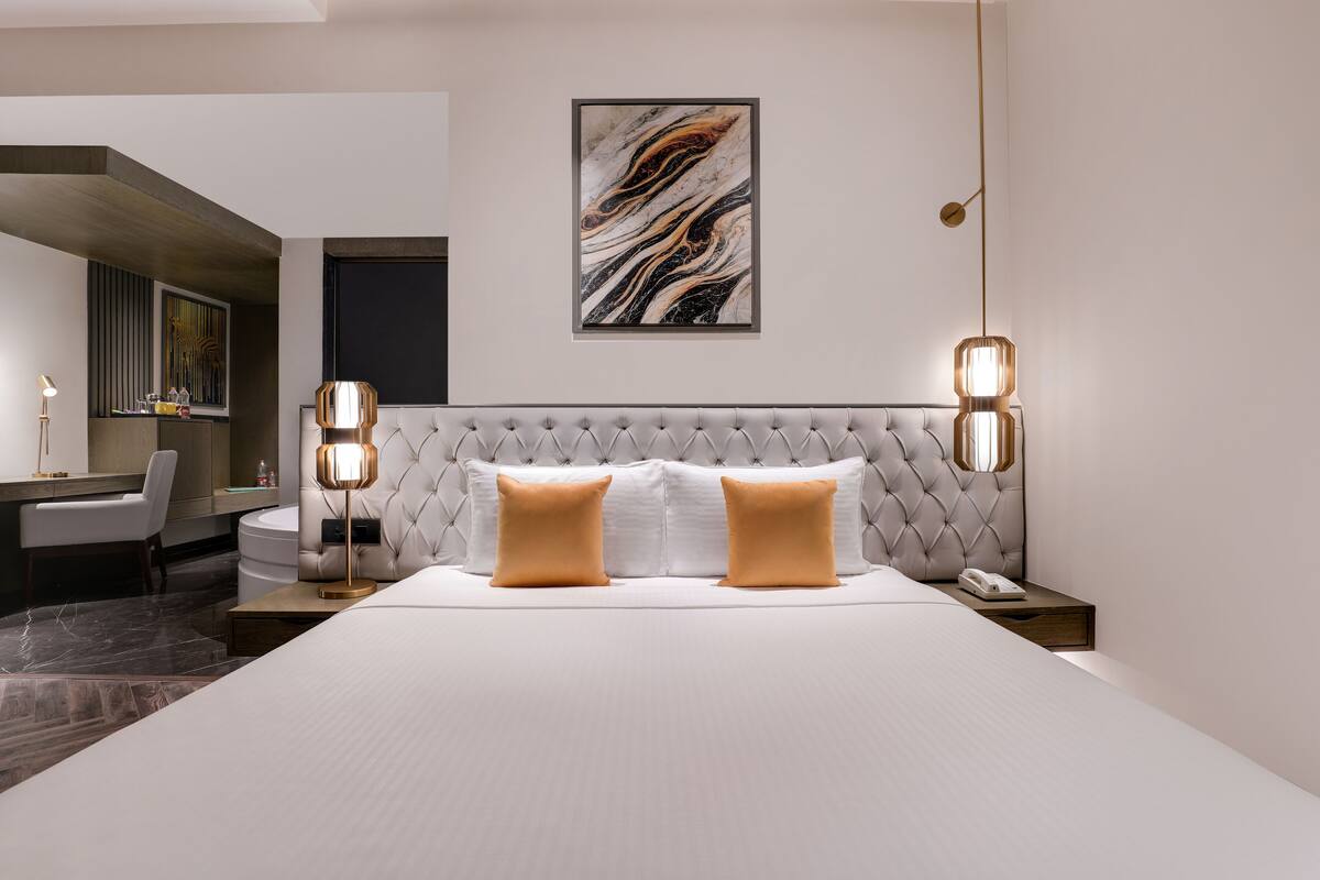 Quarto de hotel moderno com uma cama grande, duas luminárias de cabeceira, uma escrivaninha e uma cadeira.
