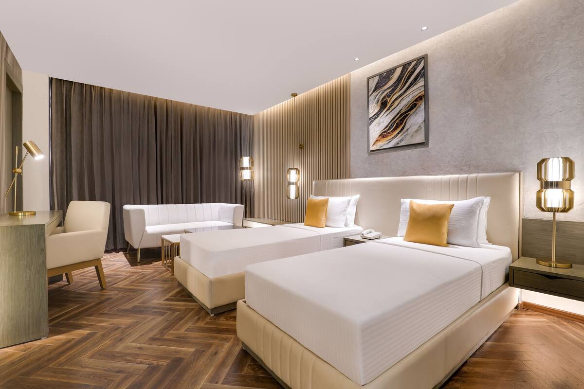 Quarto de hotel moderno com duas camas, uma escrivaninha e uma cadeira.