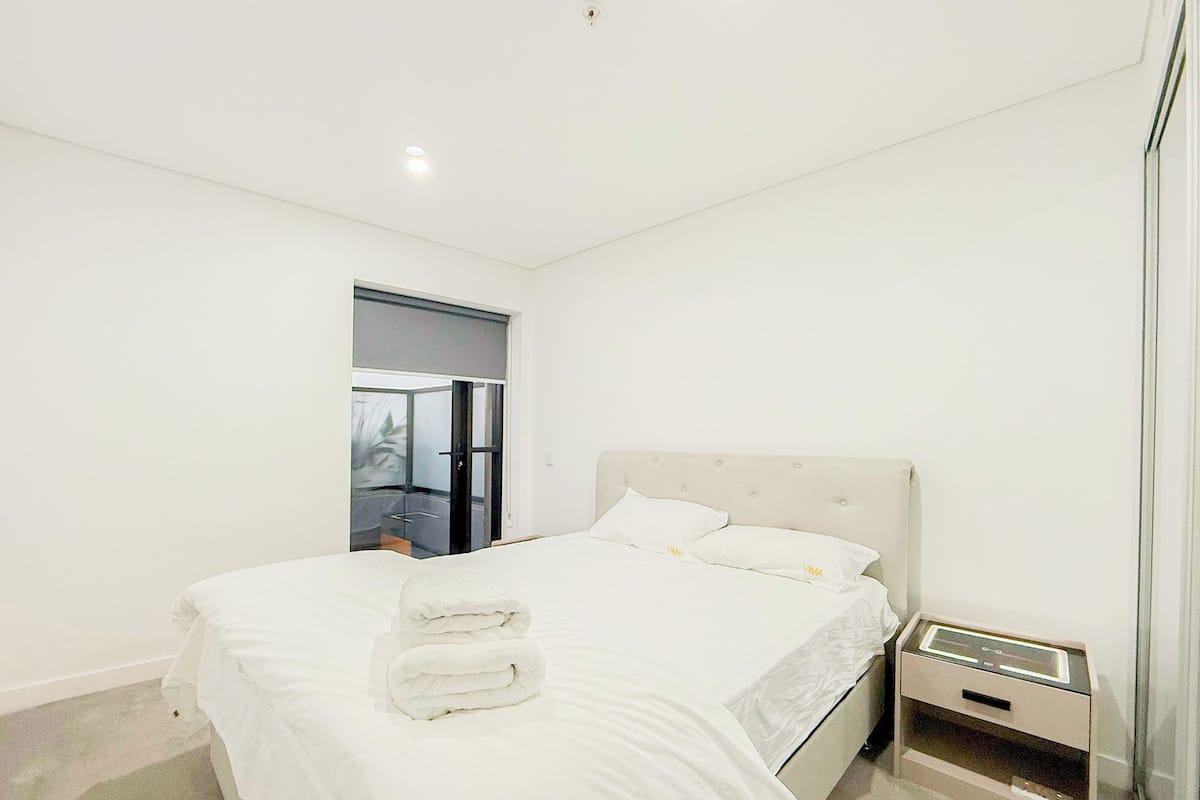 Quarto moderno com cama, mesa de cabeceira e roupeiro embutido.