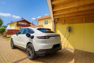 Um Porsche Cayenne branco estacionado em frente a um edifício amarelo com telhado de madeira.