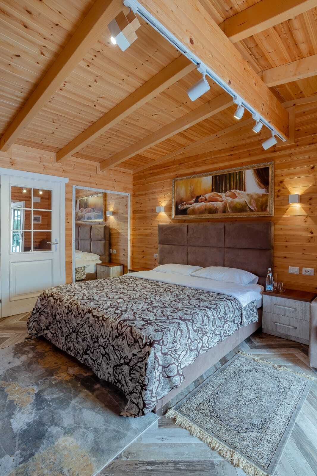 Quarto de cabana de madeira com uma cama, uma mesinha de cabeceira, um quadro e uma escada.